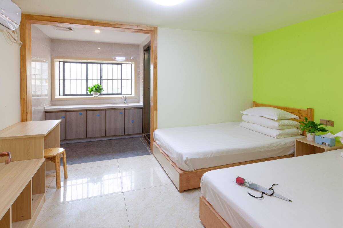 Quarto com duas camas, uma escrivaninha, uma cadeira, uma janela e uma pia.