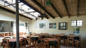 Um quarto com mesas e cadeiras de madeira, um telhado de palha e várias imagens emolduradas nas paredes.