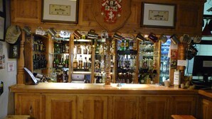 Um bar com painéis de madeira, prateleiras com garrafas de bebidas e um aviso para gorjetas aos funcionários.