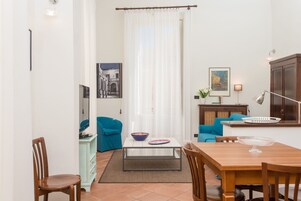 Uma sala de estar com uma mesa de jantar, cadeiras, sofá, mesa de centro e televisão.
