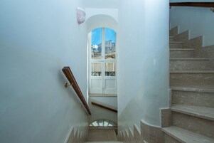 Uma escadaria com corrimão, uma janela com grade decorativa e uma porta com puxador de latão.