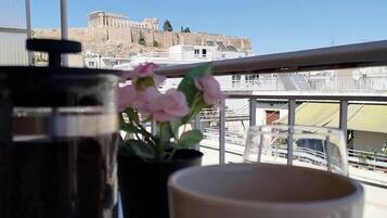Uma varanda com vista para um edifício histórico, um vaso com planta e uma cafeteira.
