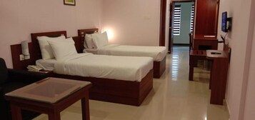 Quarto de hotel com duas camas de solteiro, uma escrivaninha, uma cadeira e uma televisão.
