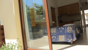 Quarto com cama coberta por um cobertor estampado, uma porta de correr de vidro que dá para uma varanda e vista para o exterior.