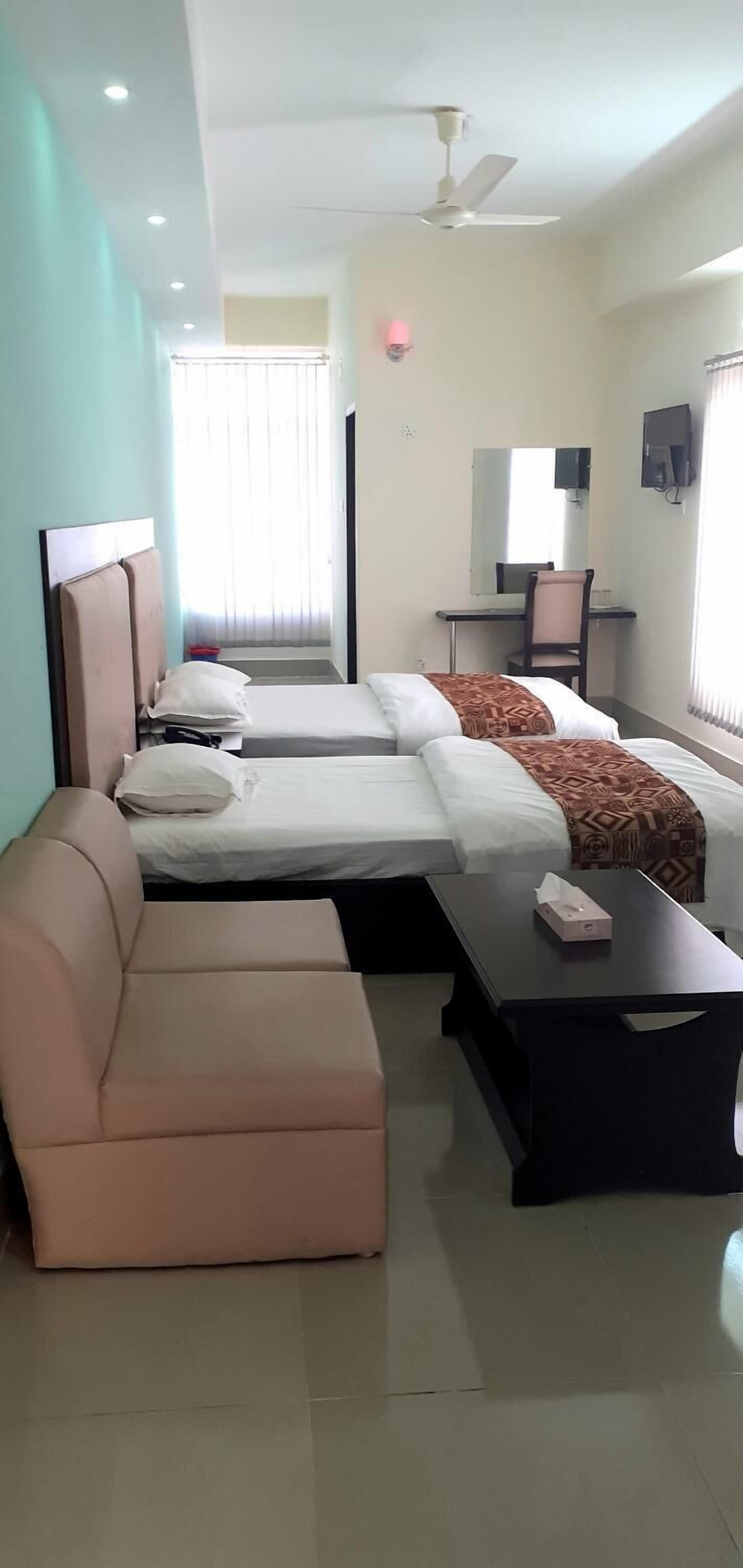 Quarto de hotel com duas camas, um sofá, uma escrivaninha e um ventilador de teto.