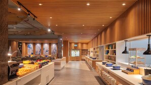 Um buffet moderno com diversas opções de comida, painéis de madeira no teto e uma disposição limpa e organizada.