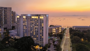 Um hotel alto com um letreiro chamativo 'OZO', área de piscina e vista para o mar com barcos.