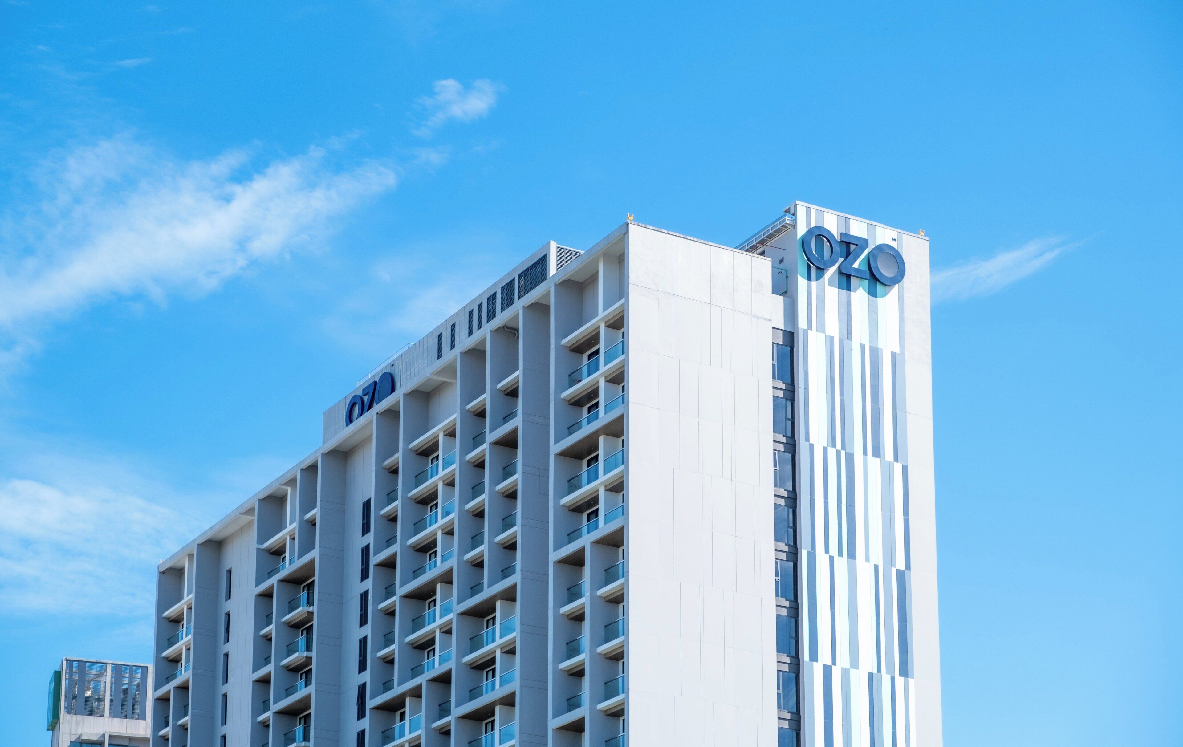 Um hotel moderno em formato de arranha-céu, com um letreiro chamativo 'OZOO' no topo.