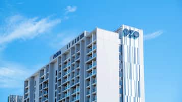 Um hotel moderno em formato de arranha-céu, com um letreiro chamativo 'OZOO' no topo.