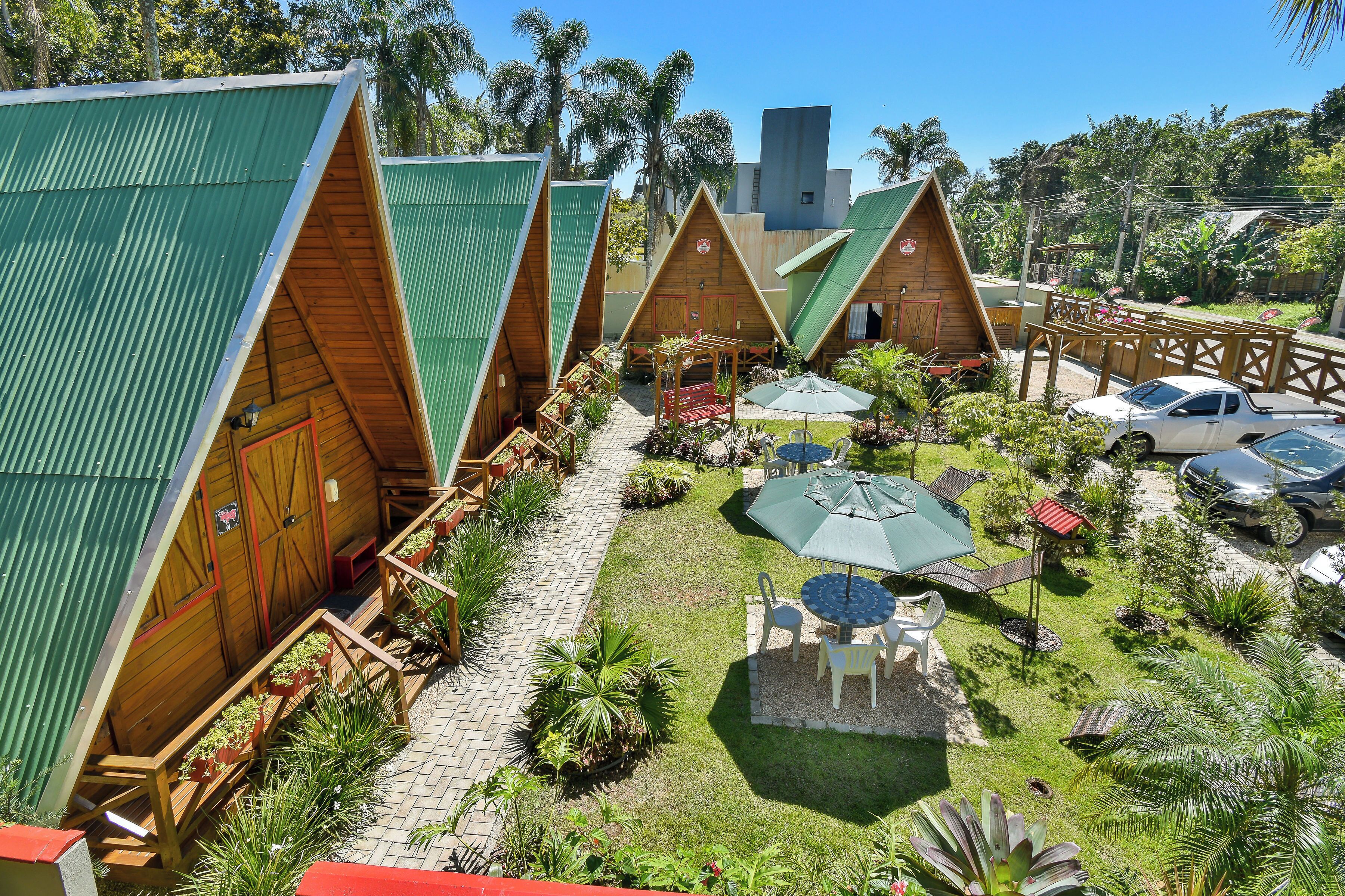 Uma fileira de cabanas em formato de A com telhados verdes, um pátio pavimentado com assentos e uma área de estacionamento.