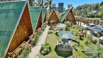 Uma fileira de cabanas em formato de A com telhados verdes, um pátio pavimentado com assentos e uma área de estacionamento.