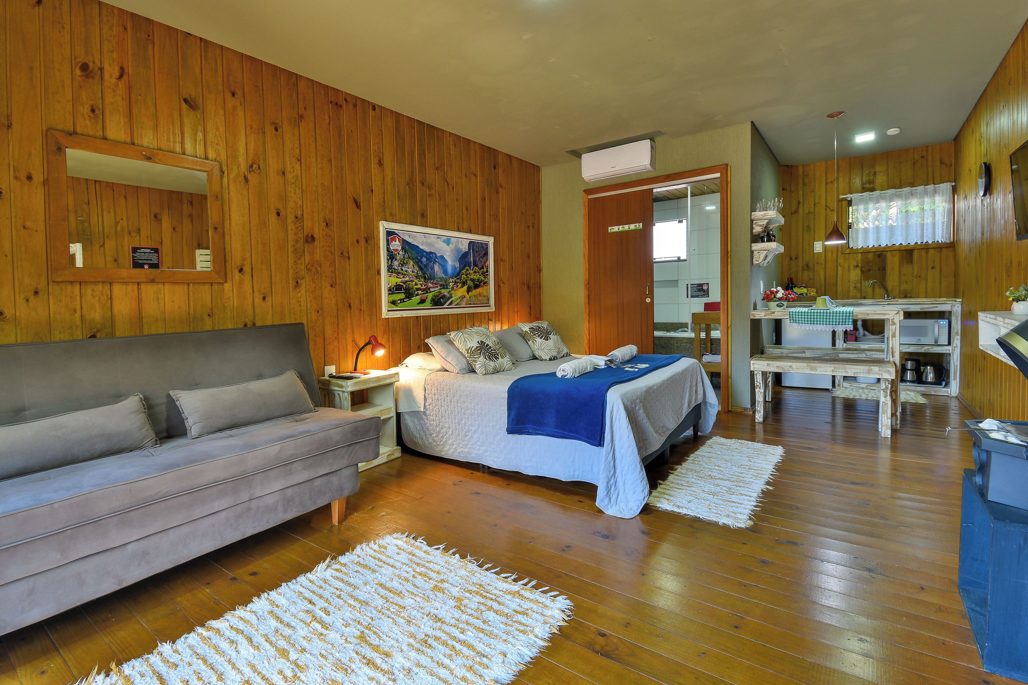 Quarto com cama, sofá, uma mesa pequena e área de cozinha com pia e bancada.