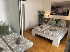 Quarto com cama, mesa de cabeceira, radiador, planta em vaso e pintura da paisagem urbana na parede.
