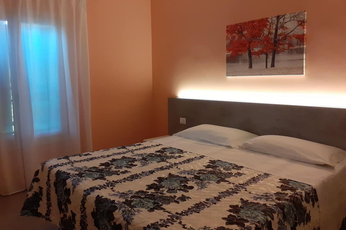 Quarto com cama, janela com cortinas e um quadro na parede.