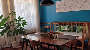 Uma área de refeições com mesa de madeira, cadeiras, luminária pendente, planta em vaso e parede azul com mapa.