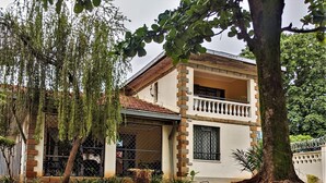 Uma casa de dois andares com varanda, cercada por vegetação e um gramado bem cuidado.