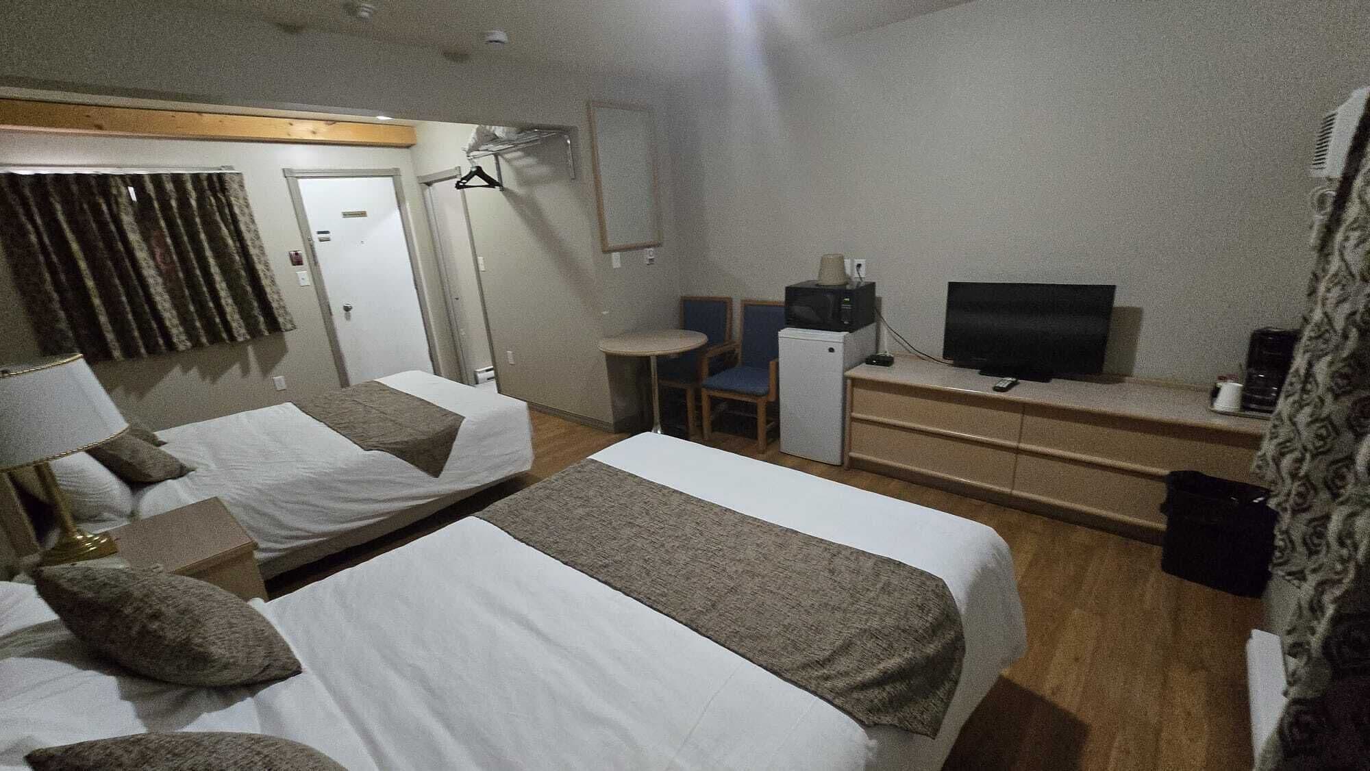 Quarto de hotel com duas camas, televisão, uma mesa pequena e um armário.
