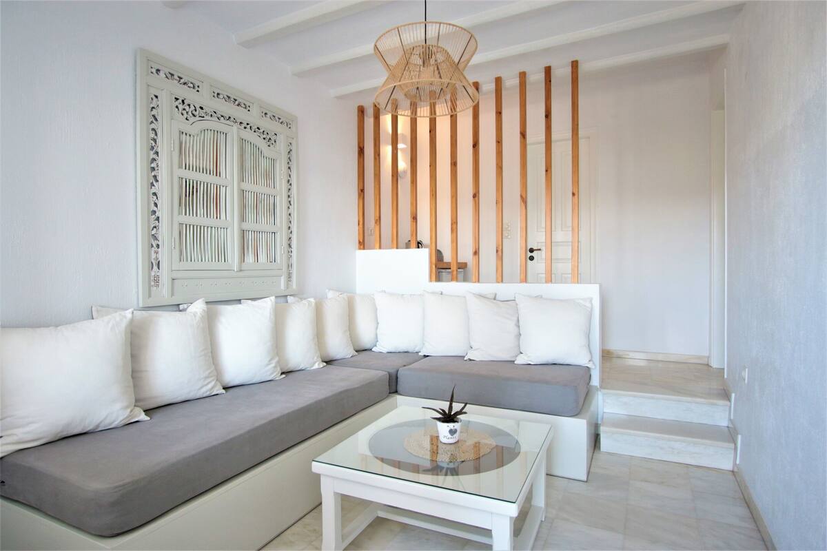 Uma sala de estar moderna com um sofá modular cinza, uma mesa de centro de vidro e um painel decorativo na parede.
