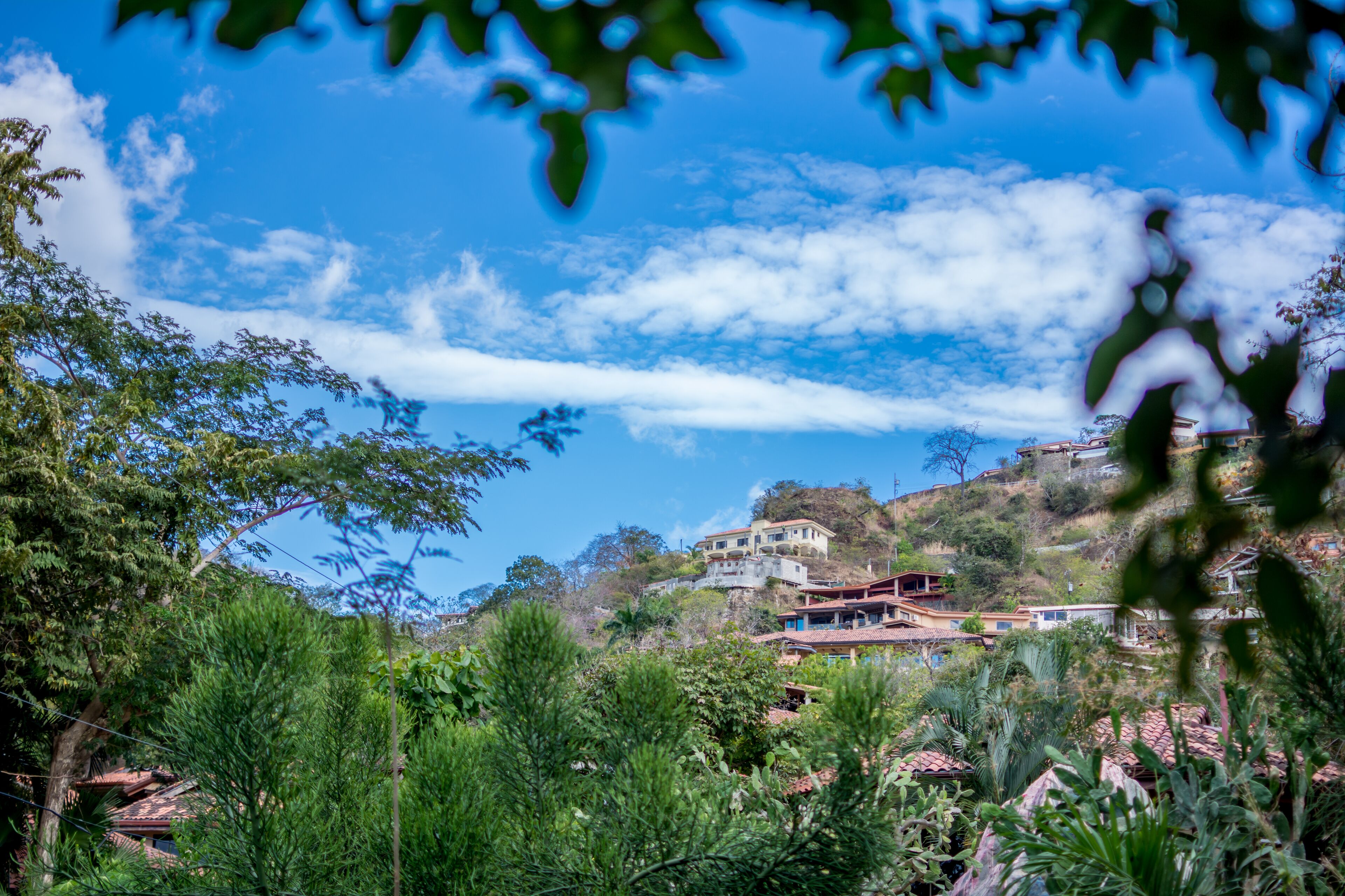 Área residencial em encosta, com casas, vegetação exuberante e céu azul límpido.