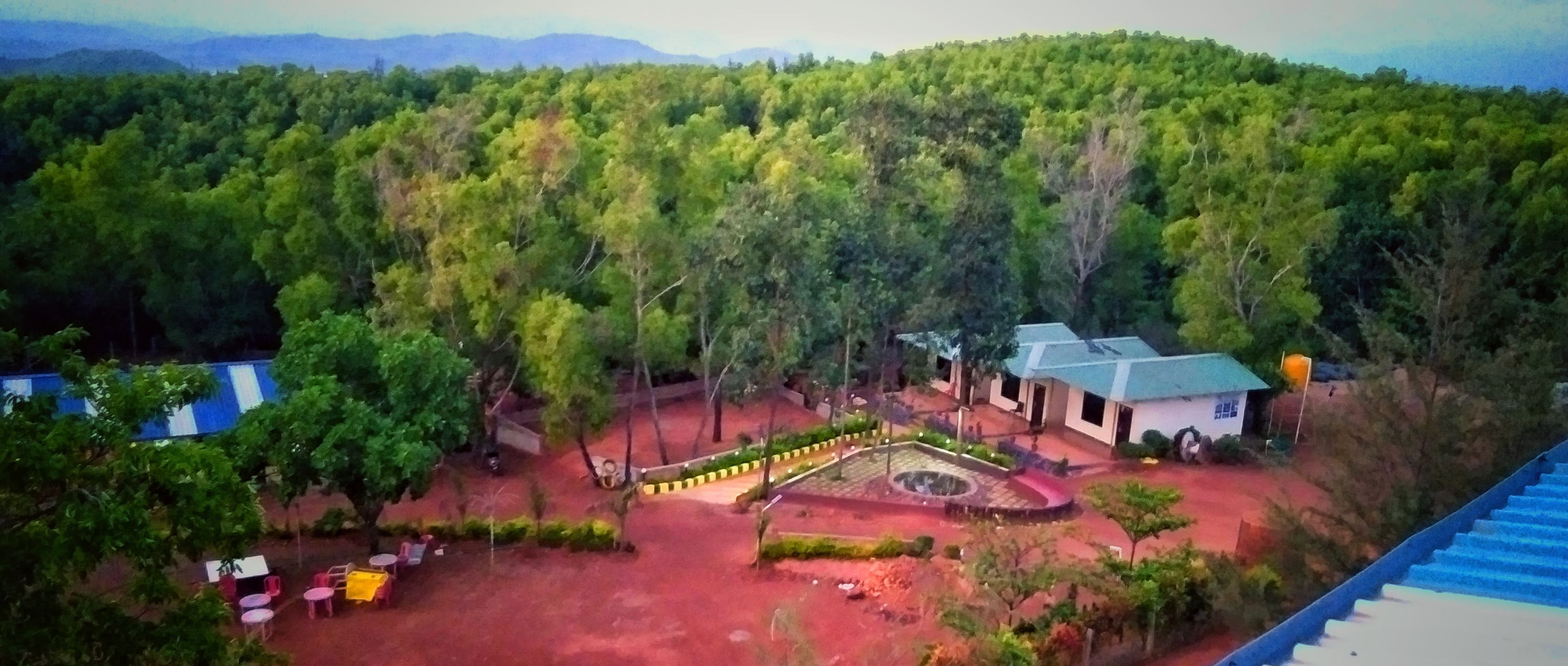 Vista aérea de um hotel com um jardim paisagístico, piscina e vista para a floresta ao redor.