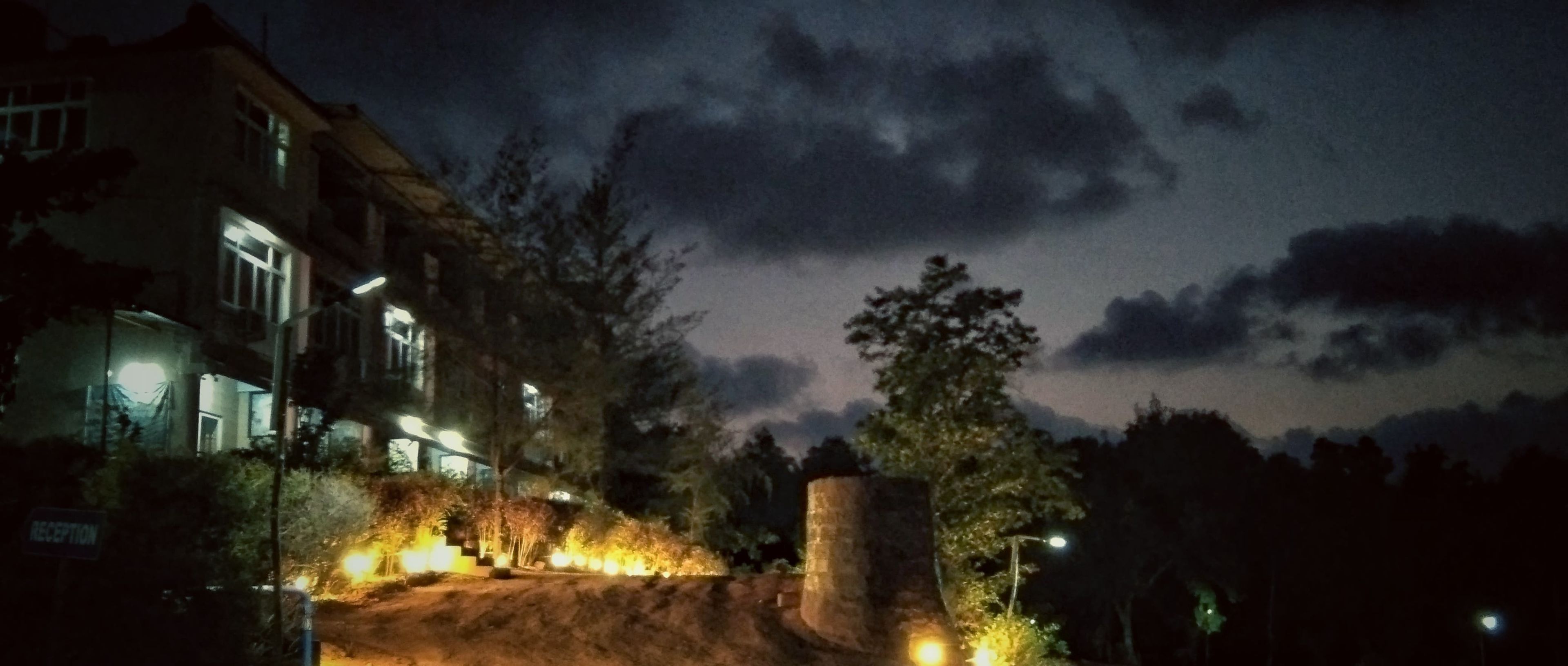 Cena noturna com uma área de recepção, um caminho de terra que leva a um edifício e uma construção de pedra.
