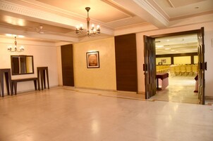 Um hall amplo com um candelabro, um quadro na parede e vista para uma área de banquetes com cadeiras.
