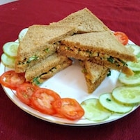 Sanduíche em um prato, com fatias de pepino e tomate ao redor.