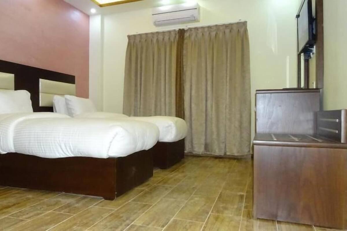 Quarto de hotel com uma cama grande, uma pequena escrivaninha e uma janela com cortinas.
