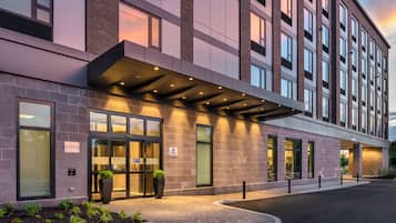 Entrada de hotel com galeria coberta, grandes janelas e placa indicando Staybridge Suites.