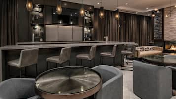 Uma área de bar moderna com um balcão comprido, vários banquetes e uma mesa de vidro redonda.
