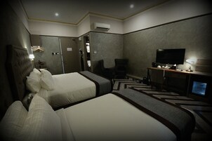 Quarto de hotel com duas camas, uma escrivaninha com televisão de ecrã plano, uma cadeira e unidade de ar condicionado.