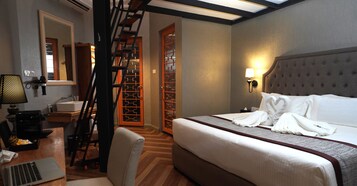 Quarto de hotel com cama, escrivaninha, laptop, cadeira, espelho e escada.