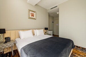 Quarto de hotel com uma cama grande, mesa de cabeceira com abajur, telefone e um quadro na parede.