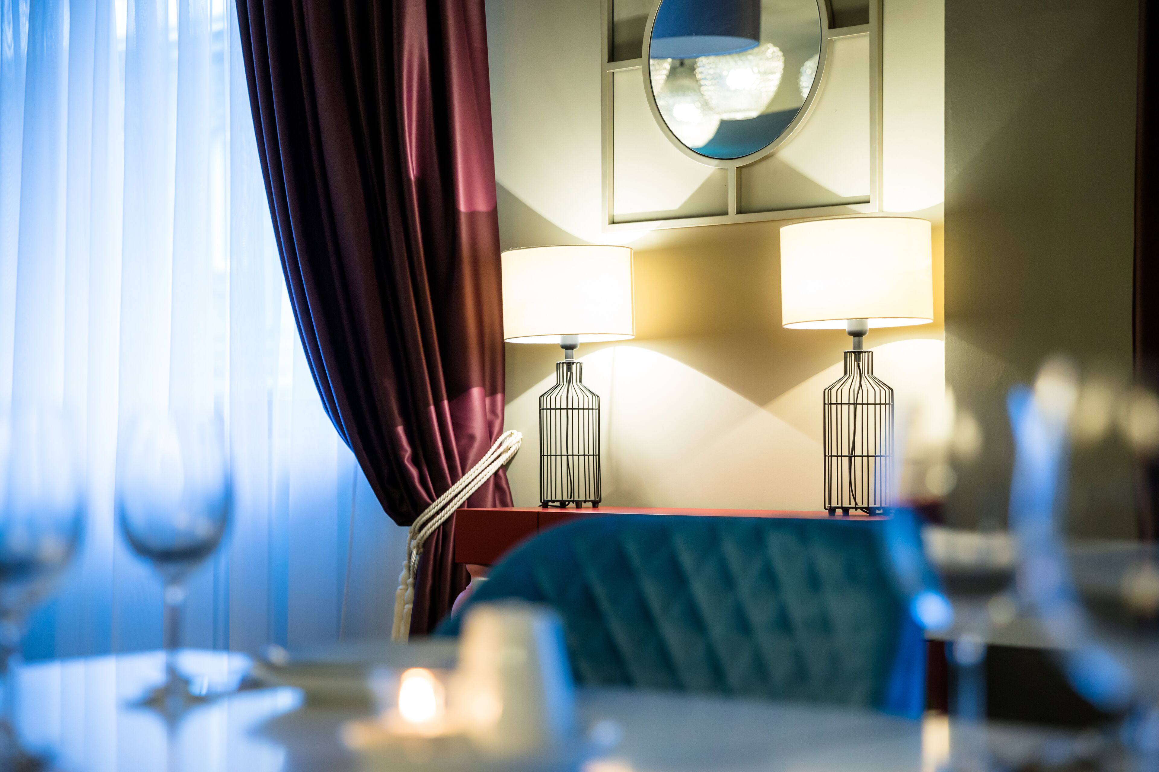 Quarto de hotel com cama, duas luminárias de cabeceira, um espelho e uma janela com cortinas.