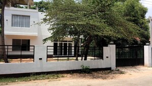 Uma casa moderna de dois andares com fachada branca, uma grande árvore na frente e um portão de metal preto.