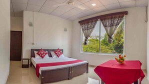 Quarto com uma cama, uma mesa com toalha vermelha e uma janela com cortinas.