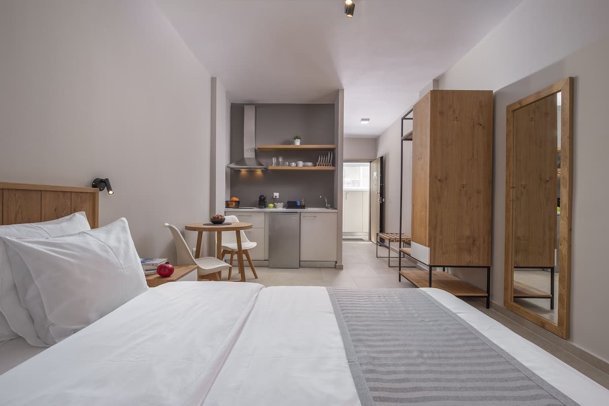 Quarto de hotel moderno com uma cama grande, uma kitchenette pequena, uma área de refeições e um espelho.