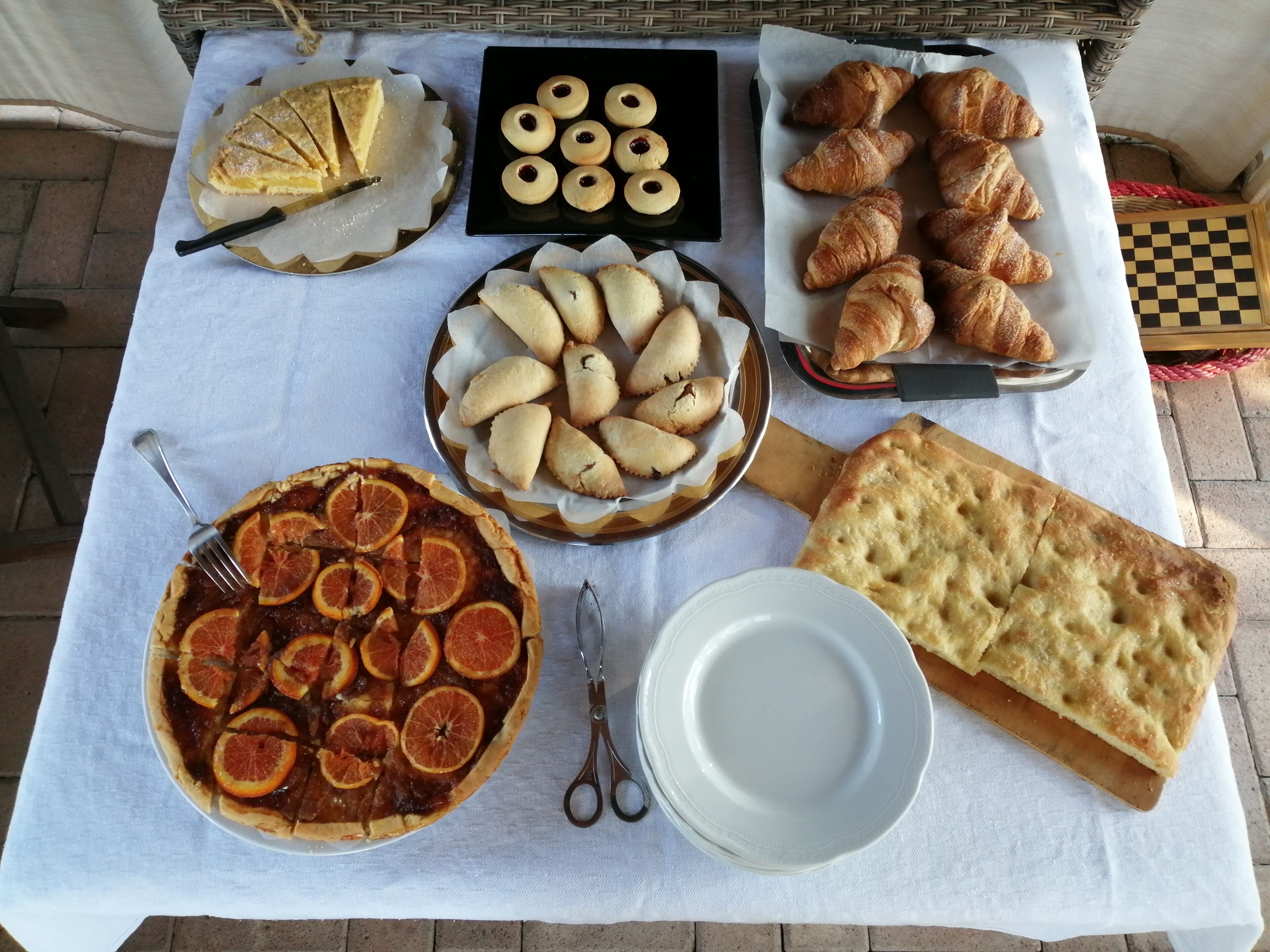 Uma mesa com diversos produtos de panificação, incluindo torta, biscoitos, croissants e pão.