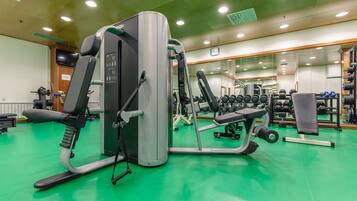 Uma academia com equipamentos de ginástica, piso verde e parede com espelhos.