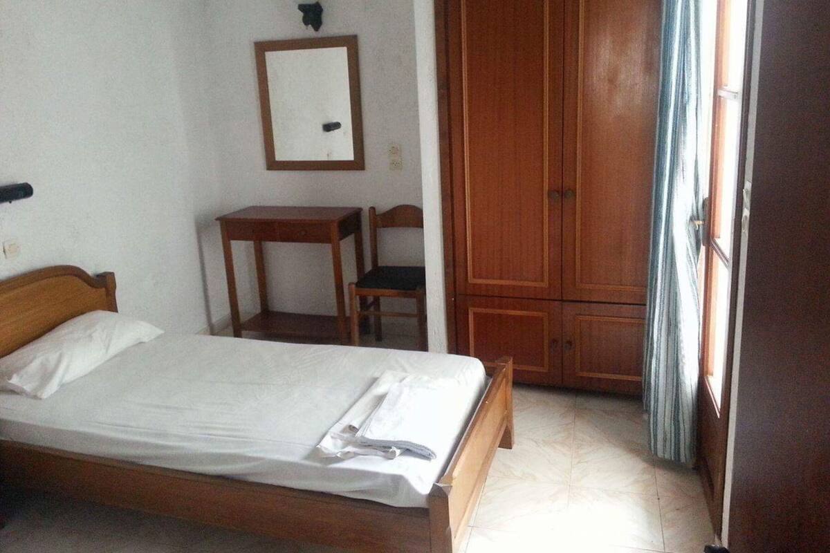 Um quarto com cama, escrivaninha de madeira, cadeira e guarda-roupa.