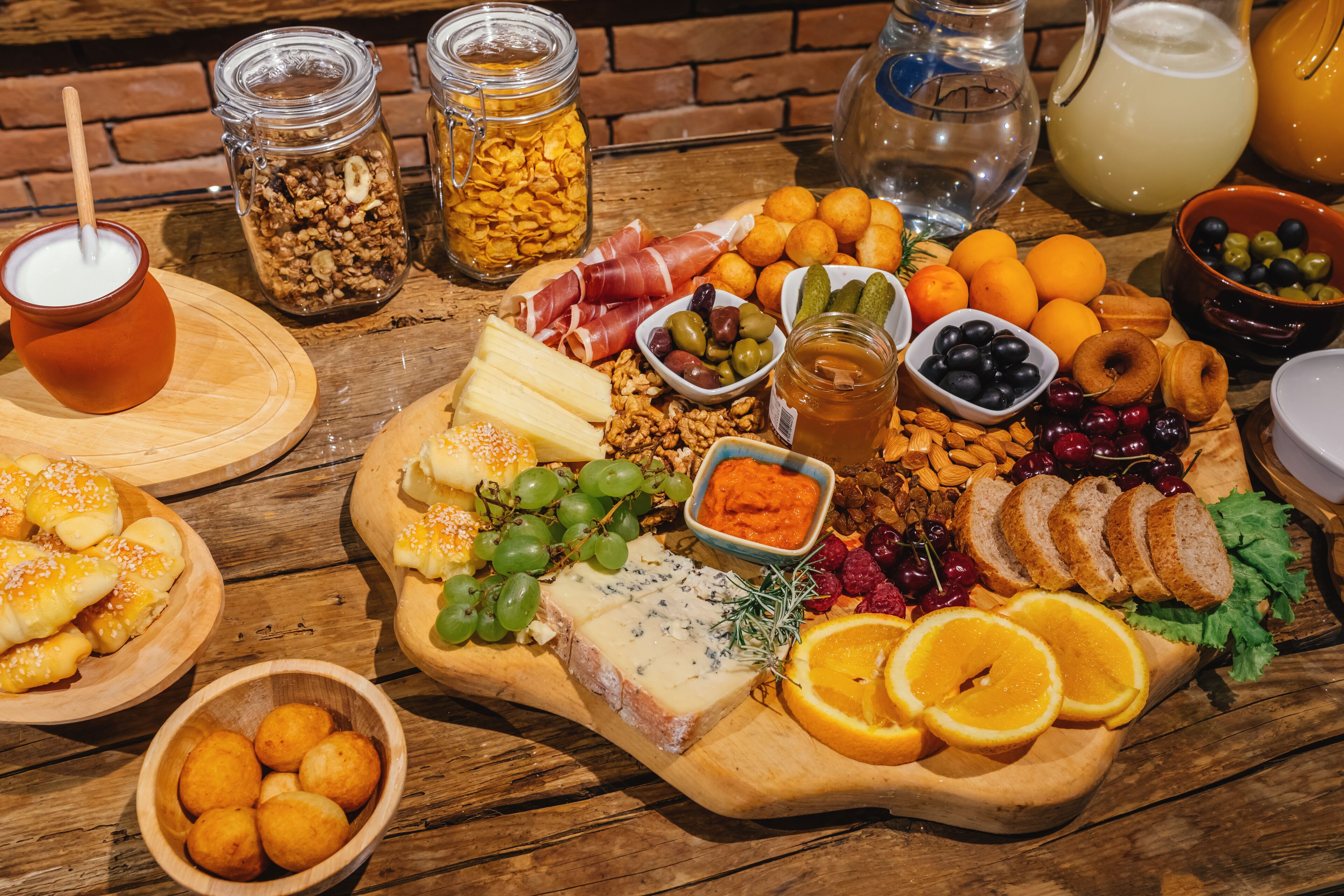 Uma mesa de madeira com diversos alimentos, incluindo queijo, frutas, nozes e pão.