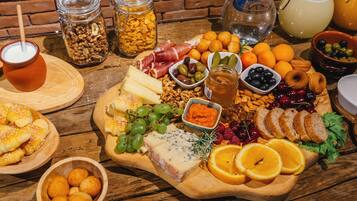 Uma mesa de madeira com diversos alimentos, incluindo queijo, frutas, nozes e pão.