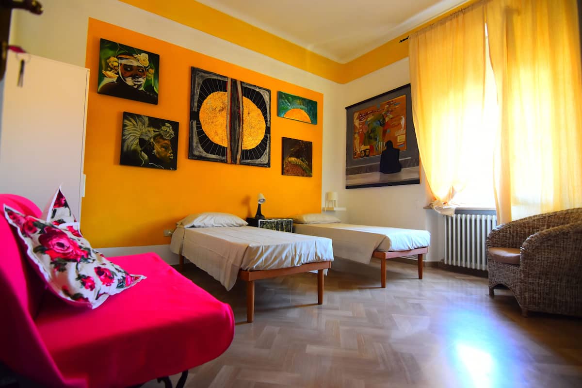 Quarto com duas camas, uma cadeira vermelha e obras de arte nas paredes.