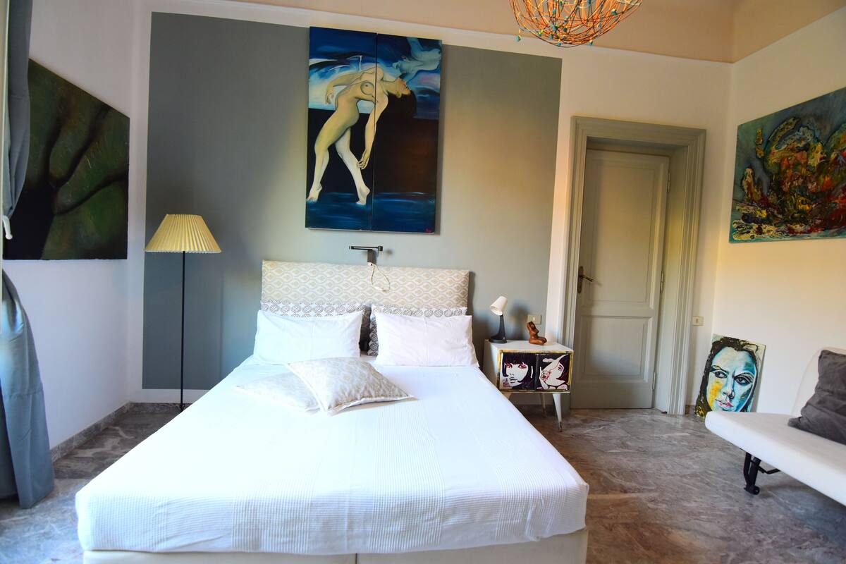 Quarto com cama grande, mesa de cabeceira com abajur e obras de arte nas paredes.