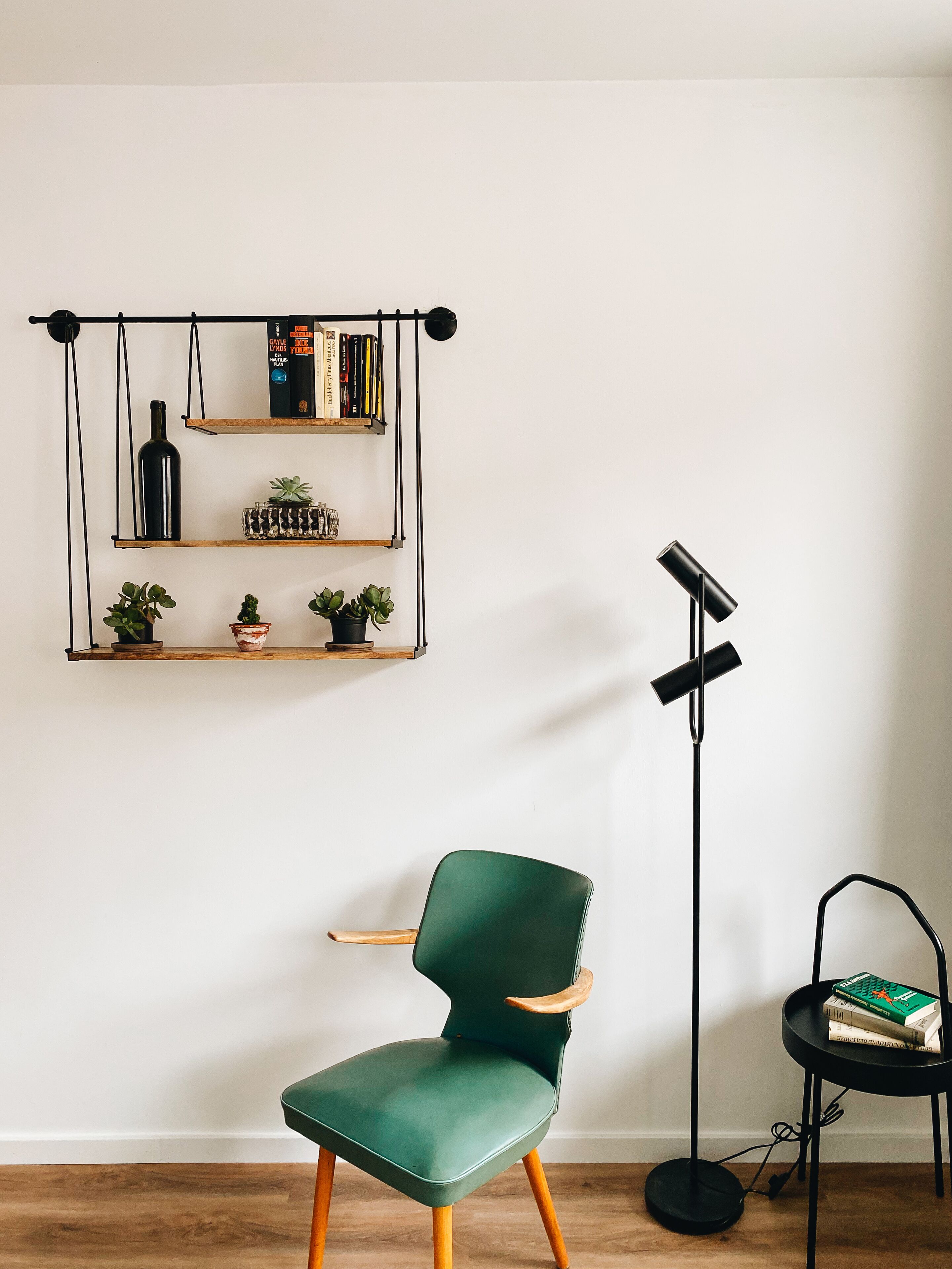Um quarto com uma poltrona verde, um abajur e uma estante de livros com livros e plantas.