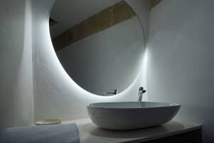 Uma casa de banho moderna com um espelho oval grande, uma pia branca e uma toalha sobre o balcão.