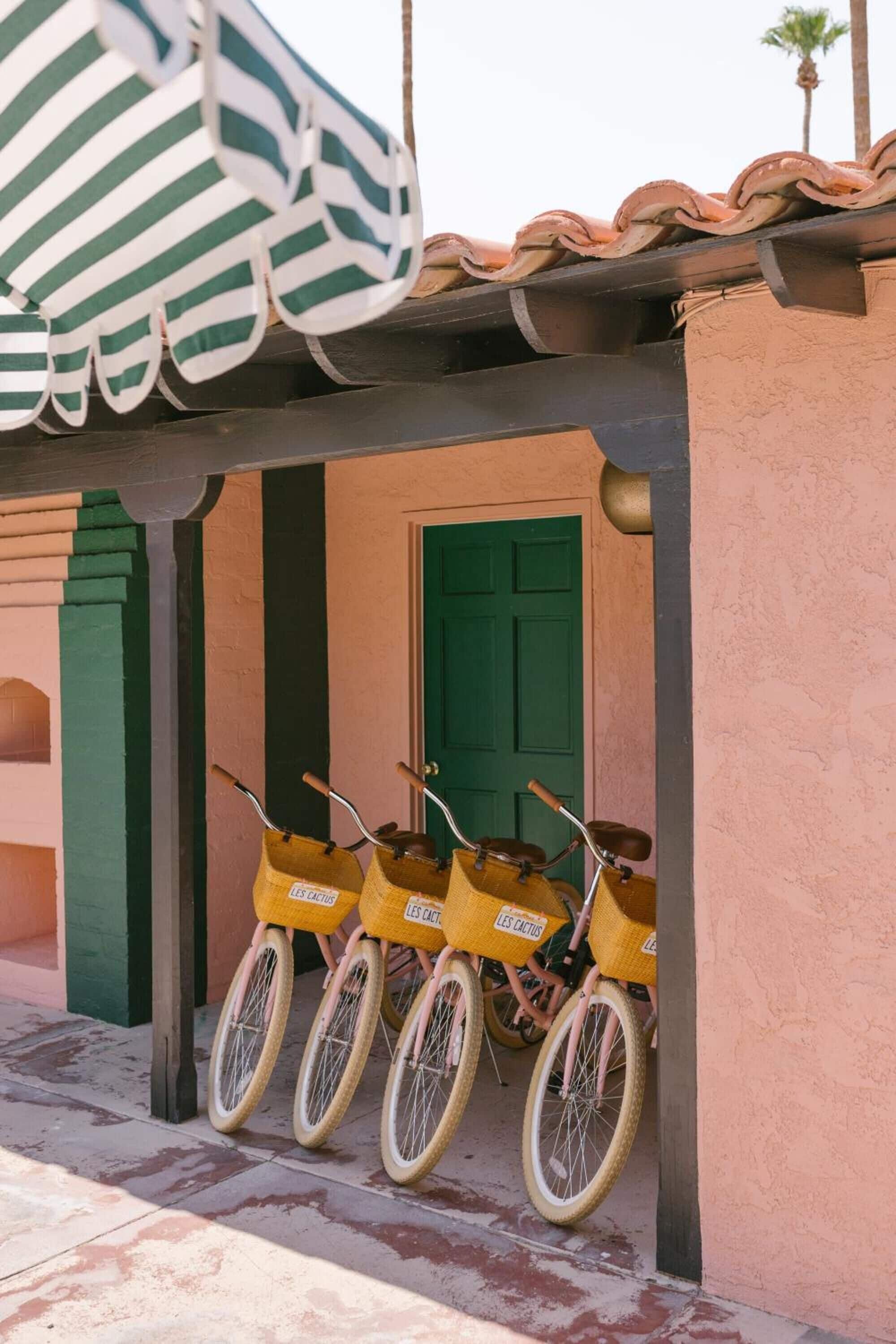 Uma fileira de bicicletas com cestas rotuladas "LES CACTUS" estacionadas sob um toldo listrado.