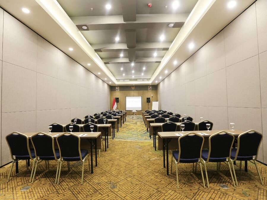 Uma sala de conferências com fileiras de mesas e cadeiras, uma tela de projetor e piso coberto de carpete.