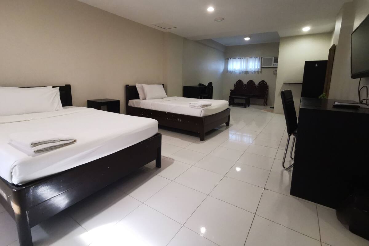 Quarto de hotel com duas camas, uma escrivaninha, uma cadeira, uma televisão e uma janela com cortinas.