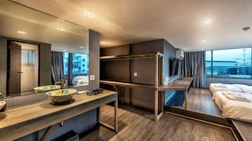 Quarto de hotel moderno com piso de madeira, um espelho grande, escrivaninha de madeira, cama e vista para a cidade.